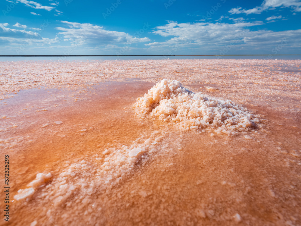 little hill of salt on the coast of pink lake under blue sky and clouds ...