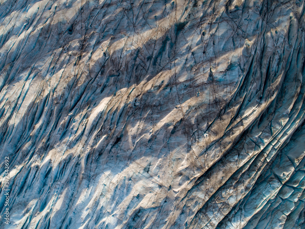 Aerial top view of the ridges of bleu and white glacier with black ash ...