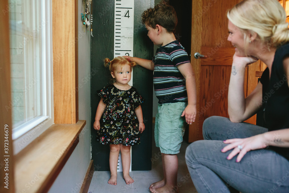 brother measure little sister on growth chart Stock Photo | Adobe Stock