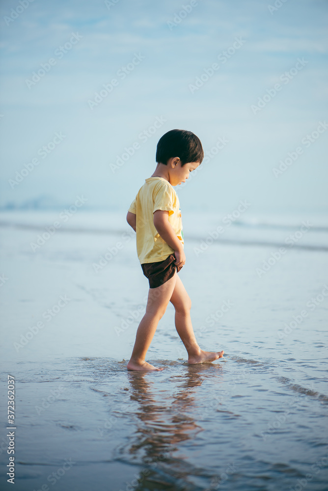 Portrait image of a boy walking on the shallow water at the beach as ...