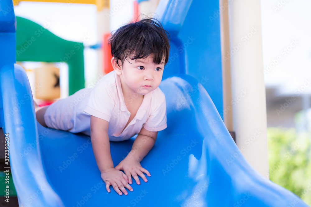 Asian toddler boy was face down to play on the blue slide. In hot day ...