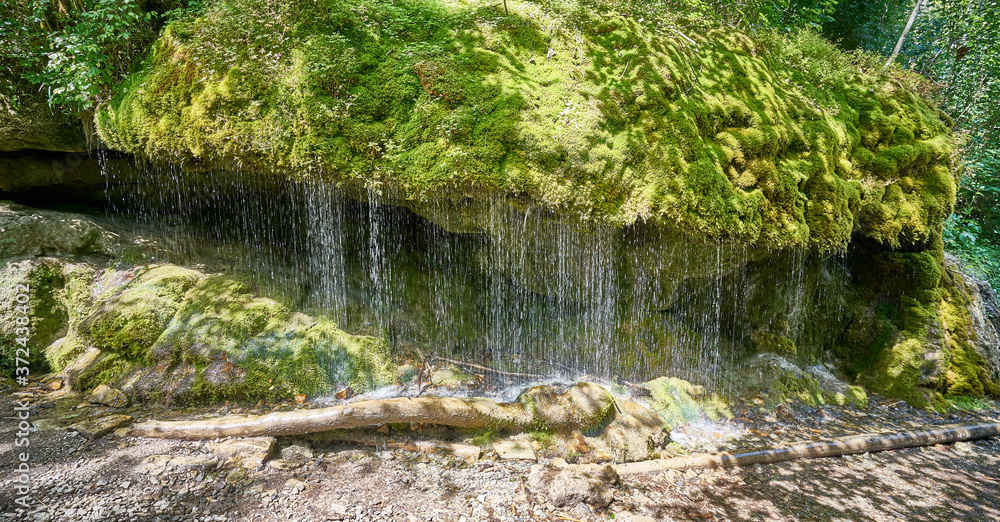 Waterfall flowing over a mossy rock with cave behind in the Canyon ...