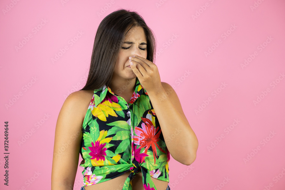 Young beautiful woman standing over isolated pink background smelling ...