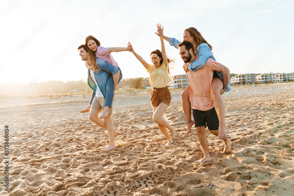 Image of young happy people having piggyback ride together by seaside ...
