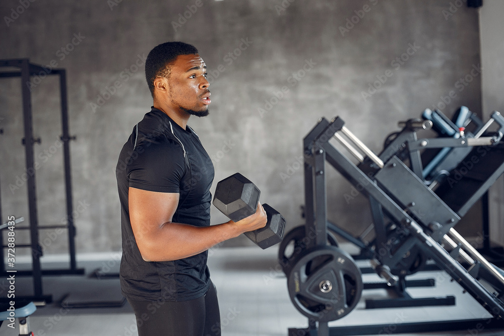 Sports man in the gym. A black man performs exercises. Guy in a black t ...
