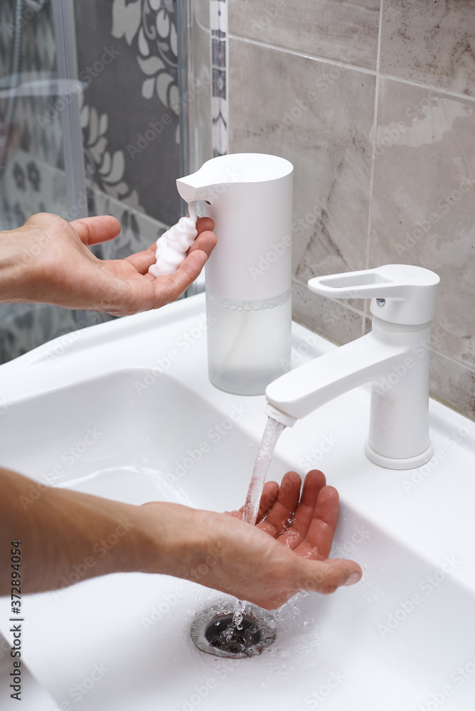 Hand washing with soapy foam from contactless dispenser in the bathroom ...