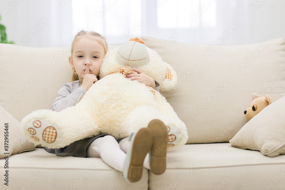 Cute little girl sitting with her legs curled up, teddy bear on her ...