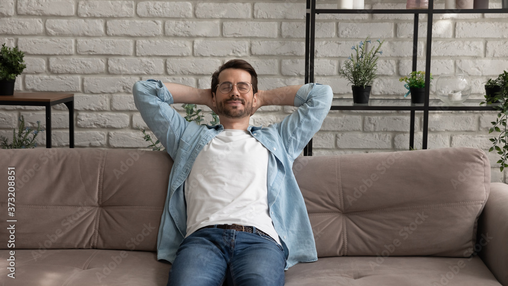 Happy young Caucasian man sit relax on comfortable sofa at home breathe ...