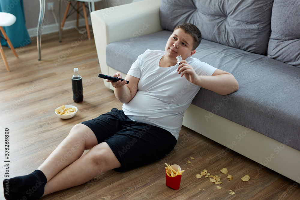 an overweight child boy enjoy leading unhealthy passive lifestyle, sits ...