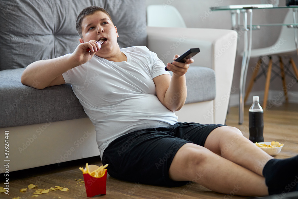 fat overweight teenager boy has bad nutrition, eat unhealthy food. sit ...