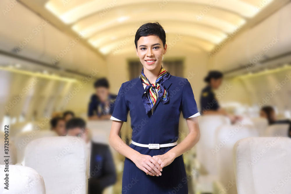Caucasian flight attendant posing with smile at middle of the aisle ...