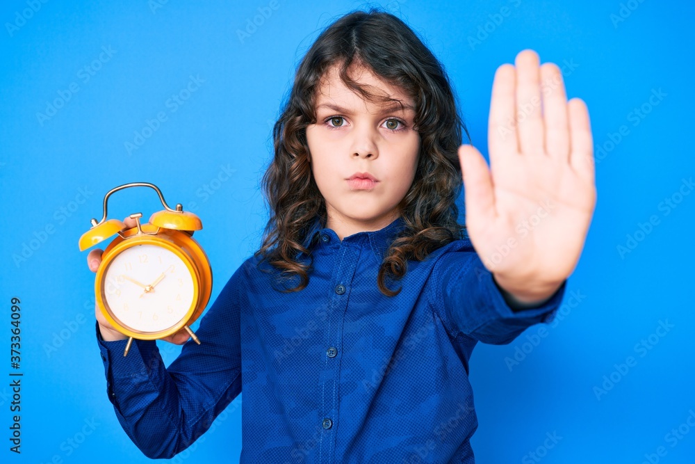 Cute hispanic child with long hair holding alarm clock with open hand ...