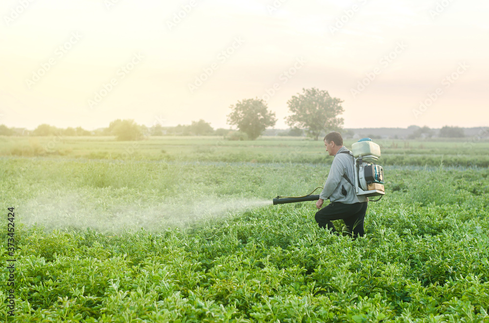 Foto de Farmer with a mist sprayer blower processes the potato ...