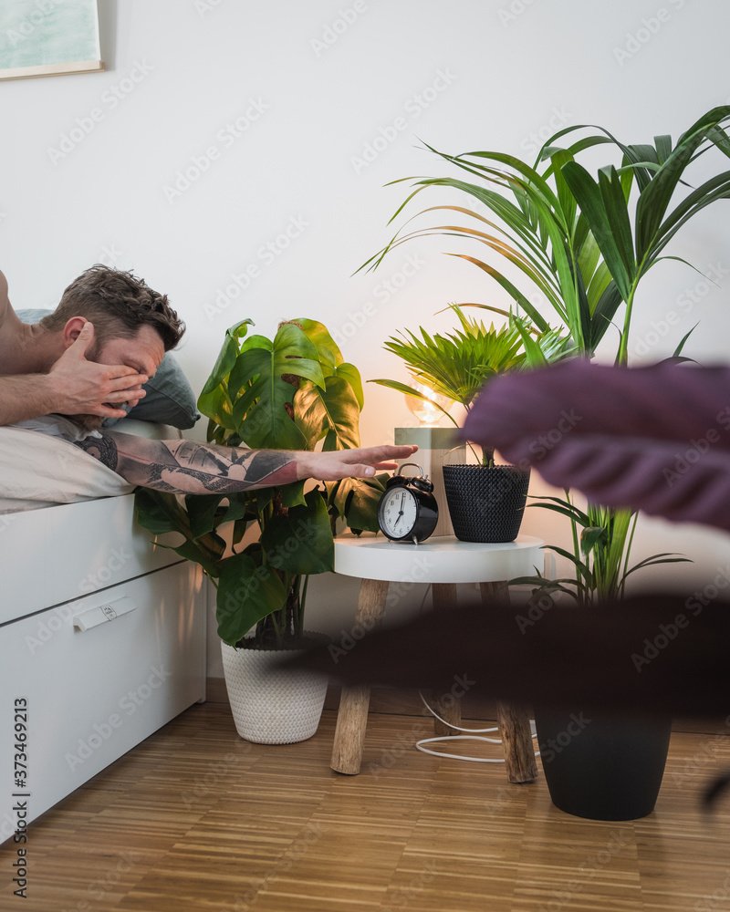 Tired man in bed trying to kill alarm clock, waking up way to early and ...