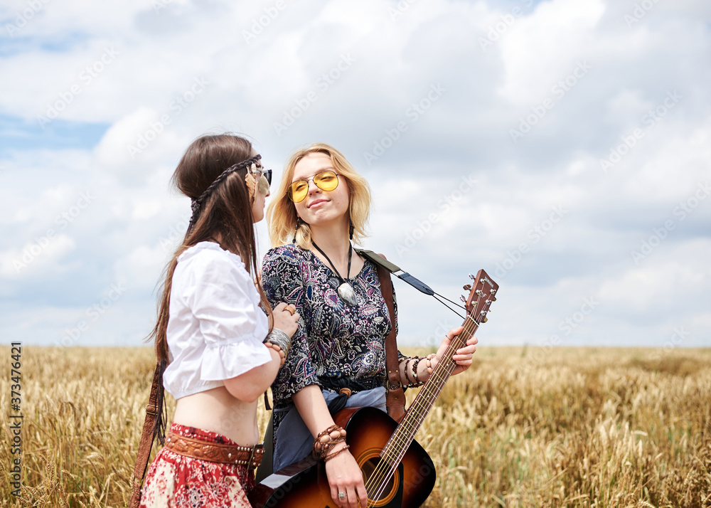 Two young skinny hippie women, wearing boho style clothes, playing ...