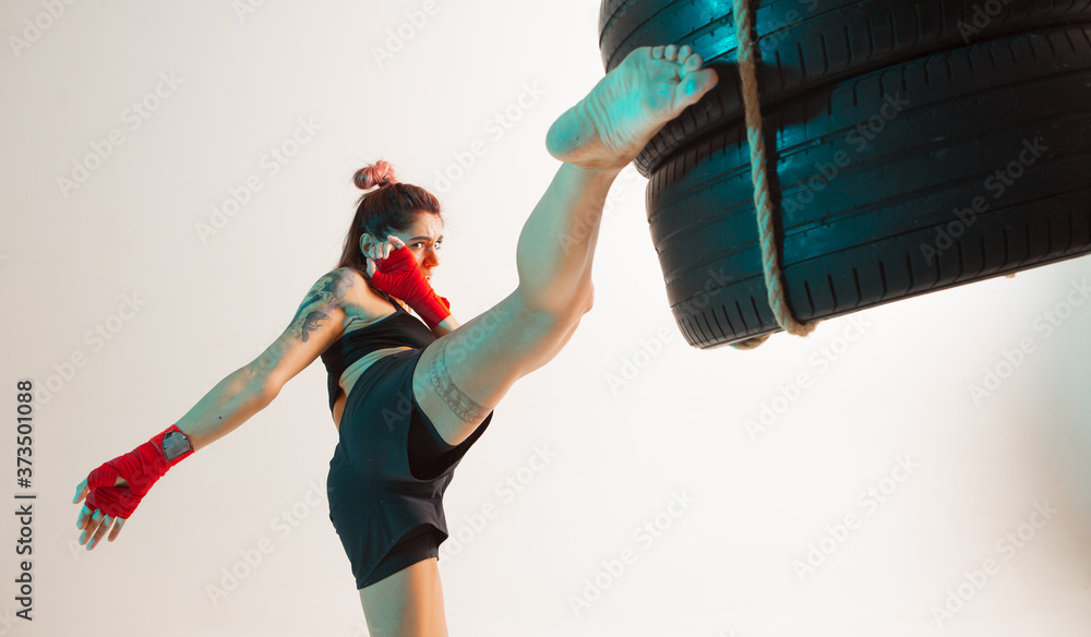 Cool girl fighter practicing kicks using tires in studio isolated on ...
