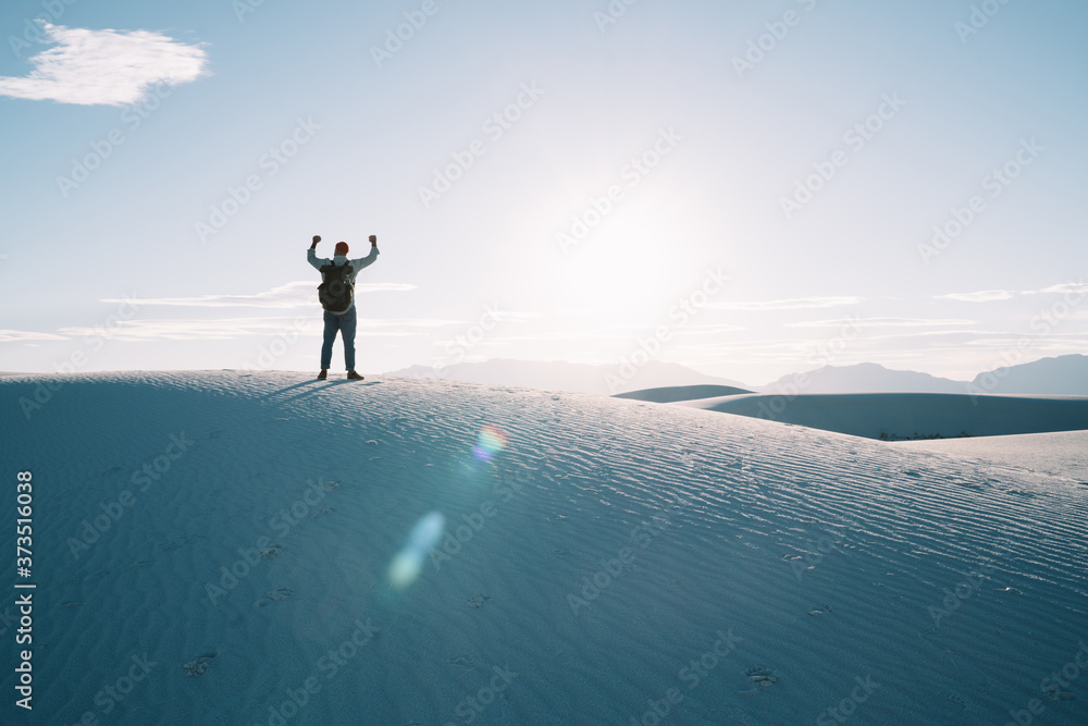 Back view of male explorer feeling victorious on top of desert dune ...