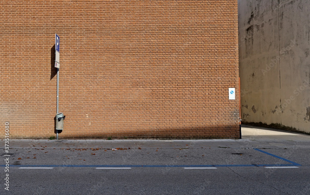 High brick wall, with sidewalk, street signs and asphalt road in front ...