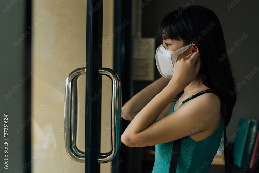 Side view of Asian woman putting on protective face covering for safety ...