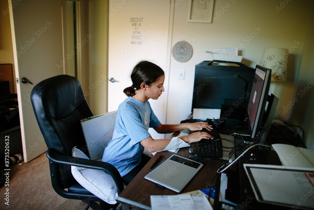 Tween girl sits at a desktop computer typing Stock Photo | Adobe Stock