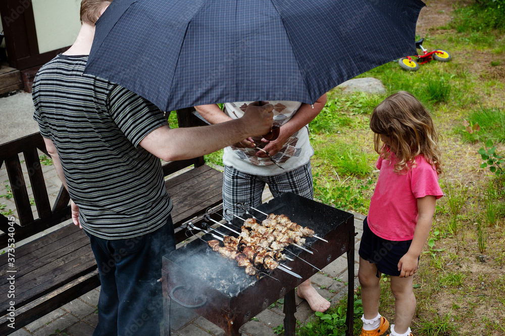 People barbecue in the rain under an umbrella Stock Photo | Adobe Stock