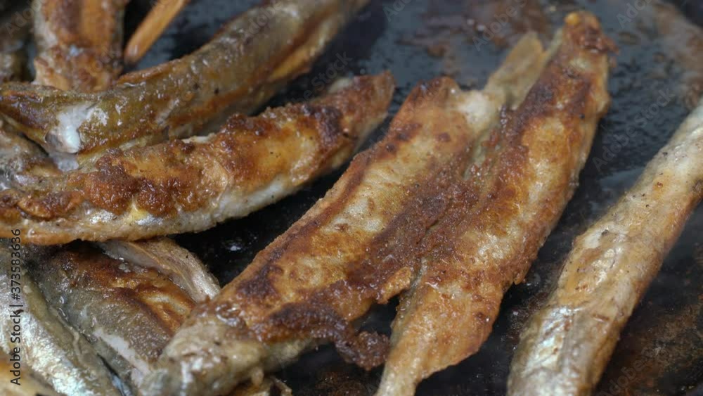 Cooking frying and stirring capelin fish fried in black pan. Close-up ...
