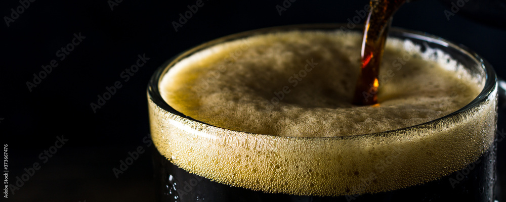 Porter beer pours from a bottle into a mug on a dark background ...