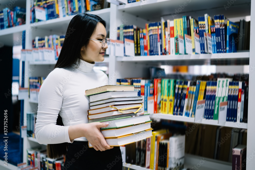 Young woman carrying pile of books in library Stock Photo | Adobe Stock
