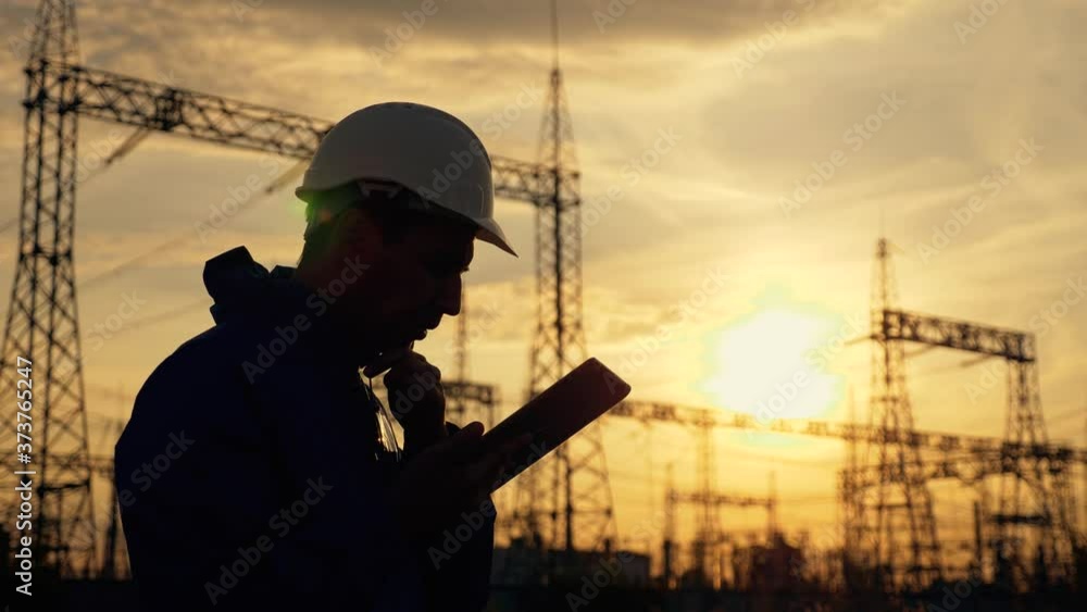 An electrical engineer wearing a helmet works with a tablet near high ...