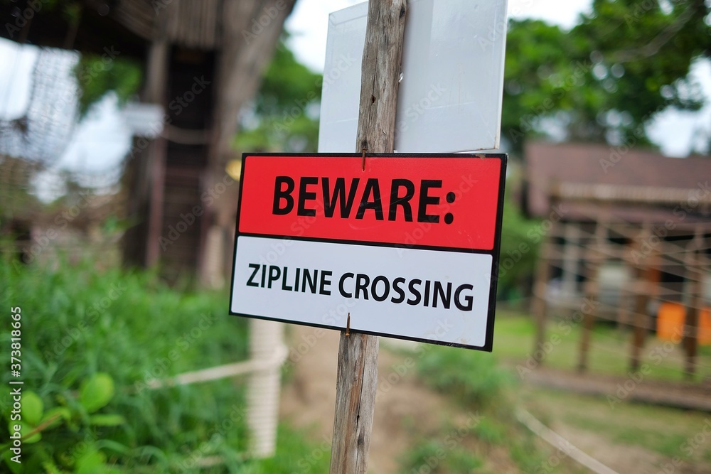 A warning along a hike trail indicating a zip line crossing up above to ...