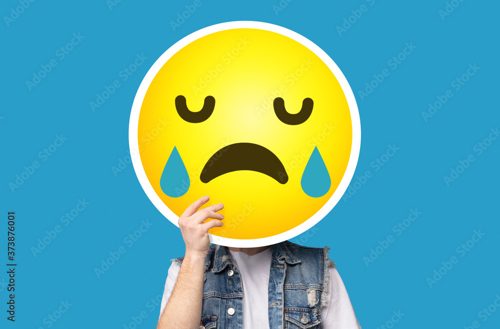 Unrecognizable man hiding his face behind crying sad emoticon emoji ...