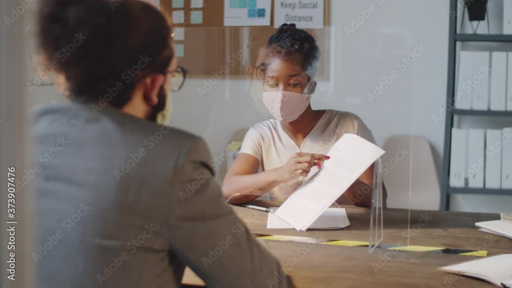 Afro-American businesswoman in face mask explaining and giving contract ...