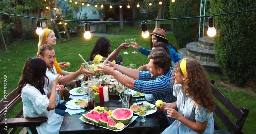 Diverse mixed races young people eating and drinking at table in garden ...
