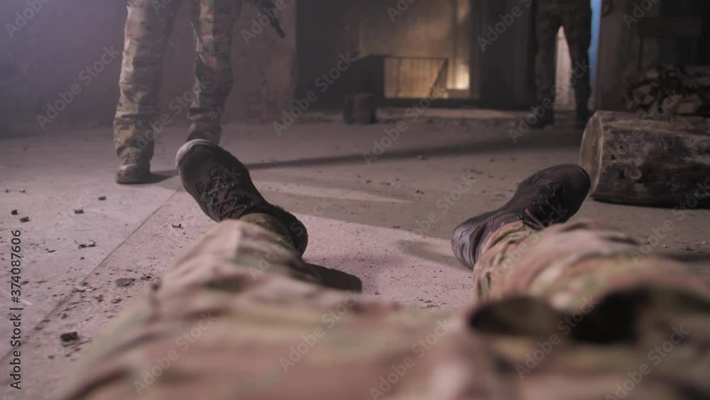 Close-up of killed soldier's legs dragging on dirty floor of abandoned ...