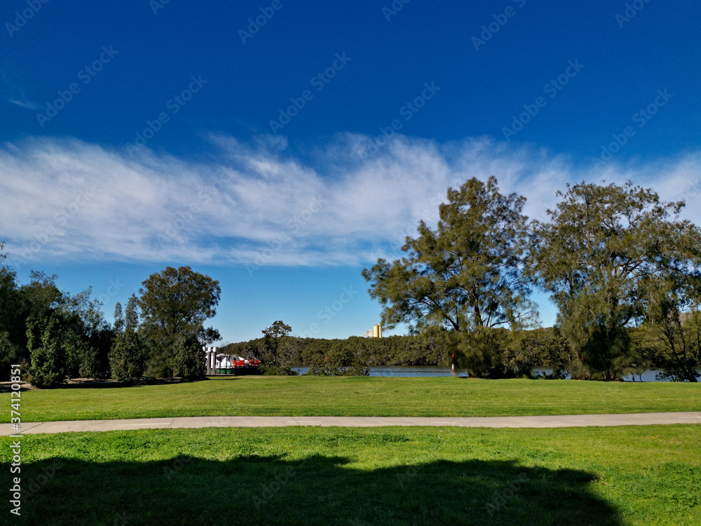 Beautiful view of a park with green grass, tall trees and paved trail ...