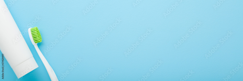 White tube of toothpaste, toothbrush with green bristles on light blue ...