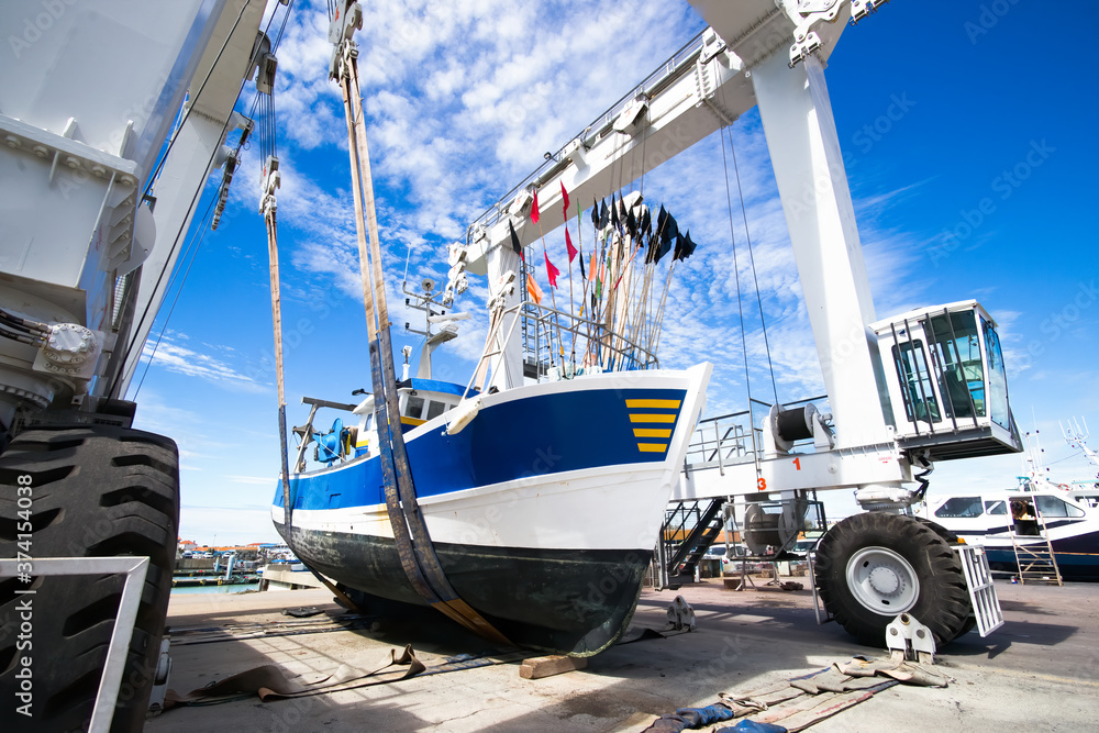 Wide angle photo of fishing boat lifted by a boat lift. Blue and white ...