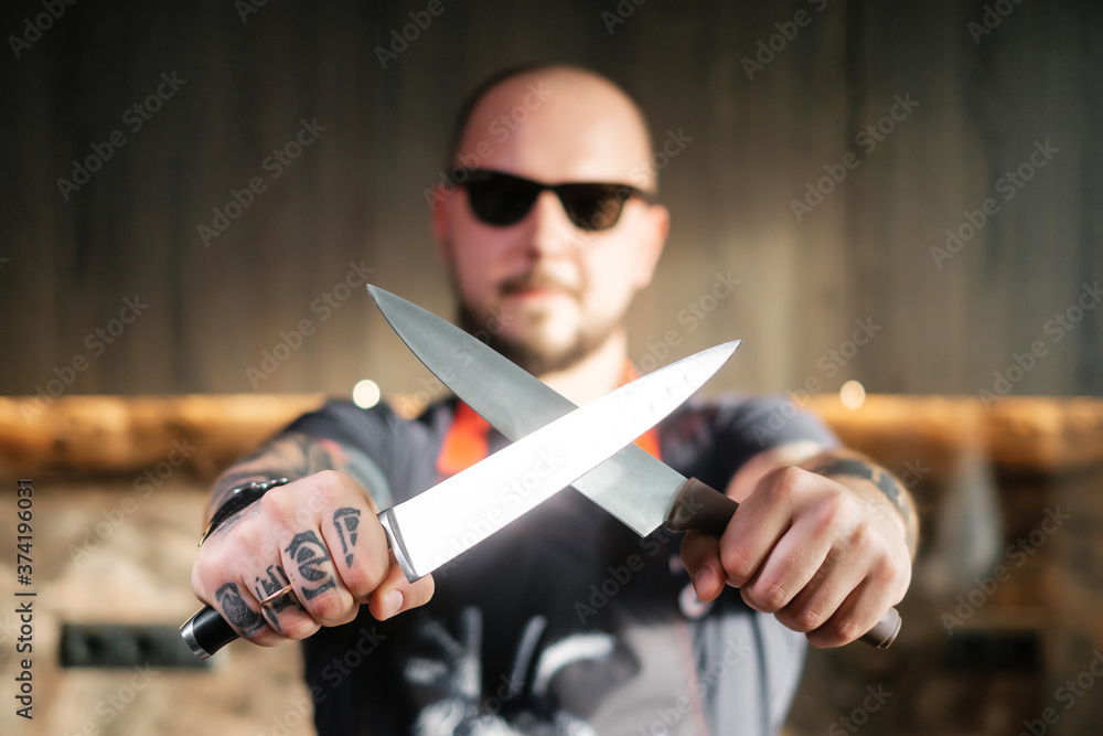 Tattooed chef with sunglasses holding sharpened knives in his hands ...