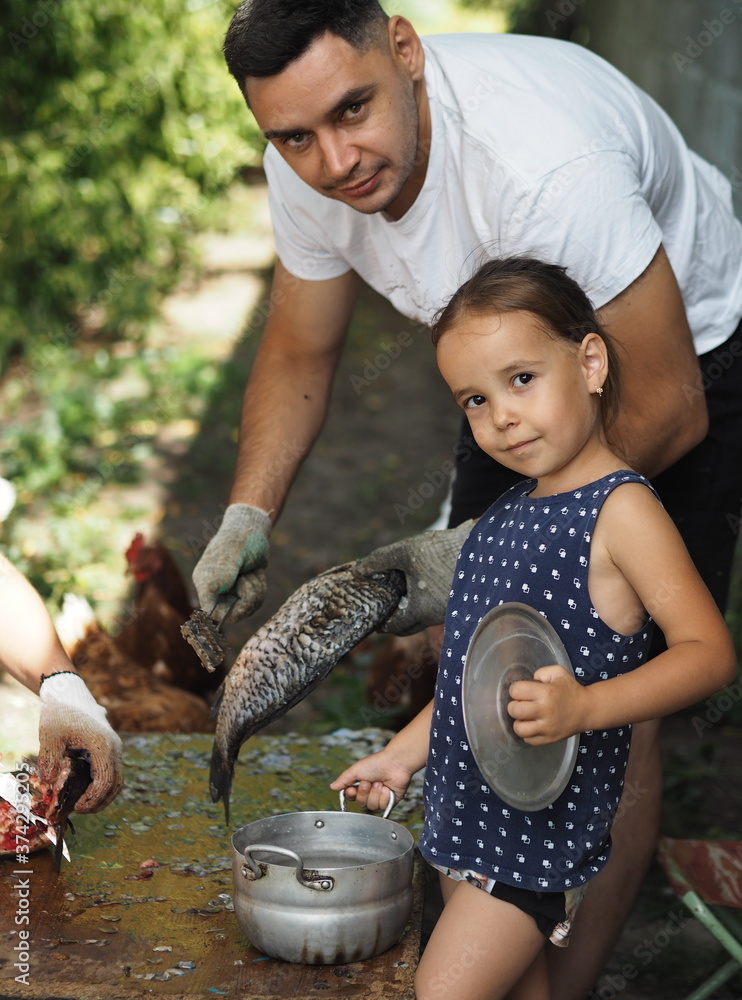Dad and daughter clean fish from scales on the territory of a private ...