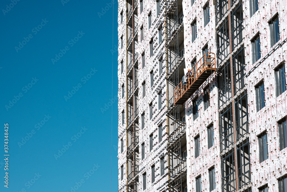 Builders on an industrial elevator are engaged in cladding and ...