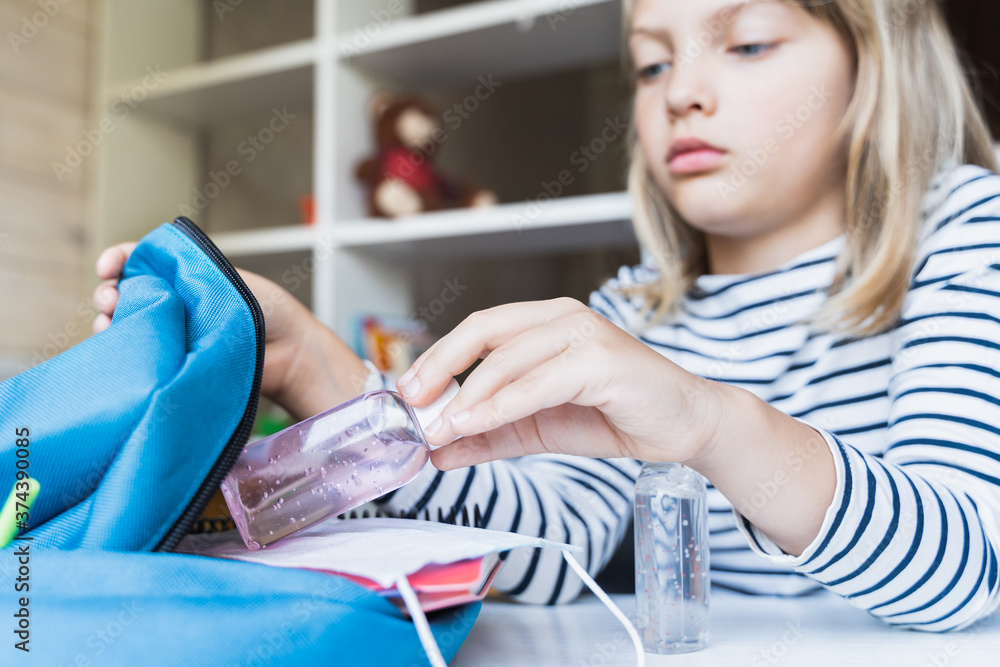 Little girl packing blue backpack in kids's room. Face mask, bottle of ...