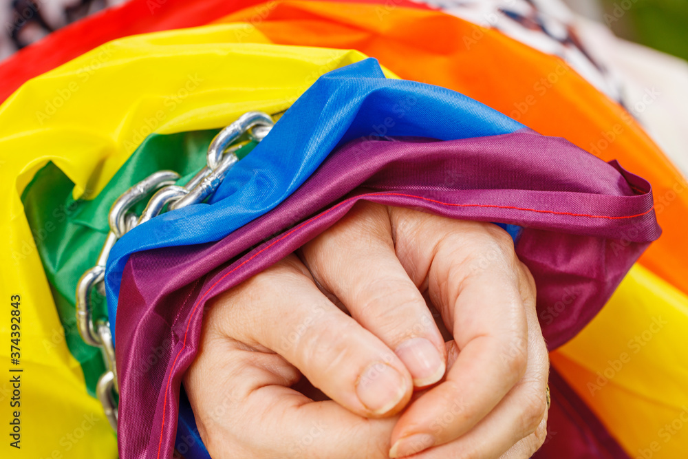 Female hands chained against the background of the LGBT flag. The ...