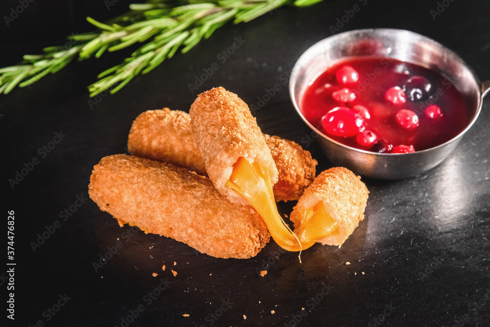Fried cheese sticks in breading with berry sauce on a black background ...