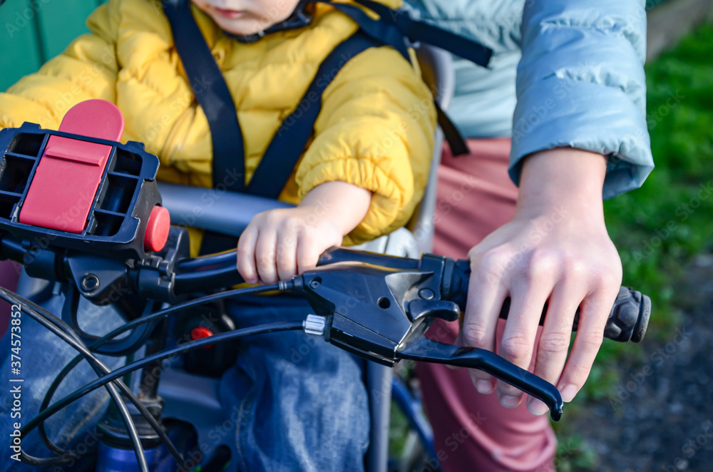 Hands of mother and child on the handlebars of a bicycle. Child in a ...