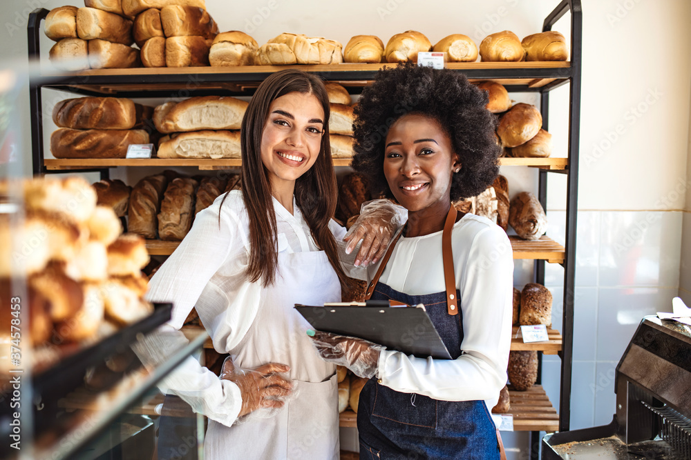 We love our job! Beautiful young women in apron standing in bakery shop ...