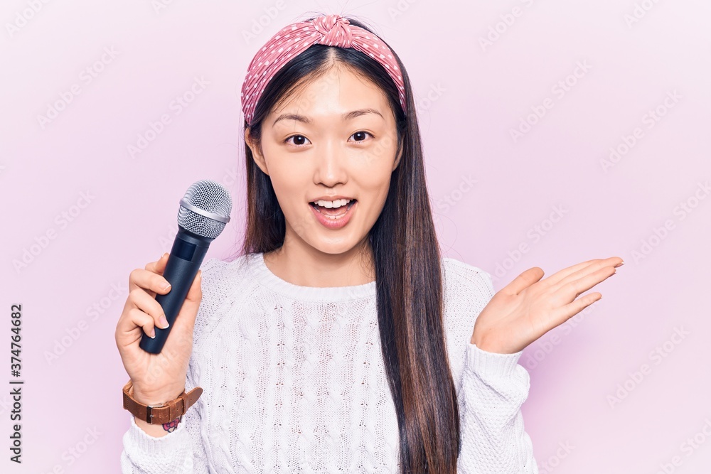 Young beautiful chinese woman singing song using microphone celebrating ...