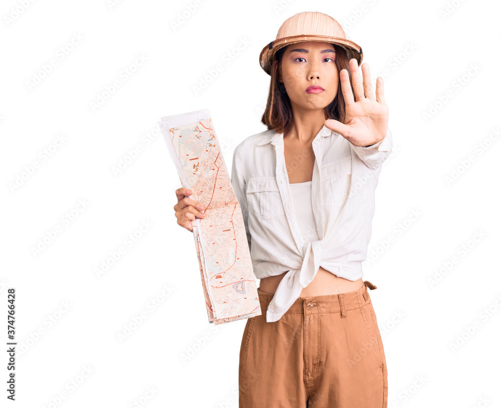 Foto de Young beautiful chinese girl wearing explorer hat holding map ...