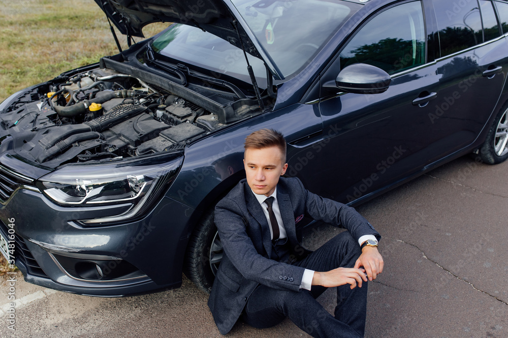 Desperate young man driver seated on the asphalt ground in front of his ...