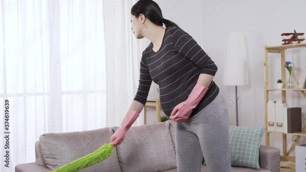 asian millennial wife holding her big belly approaching couch to remove ...