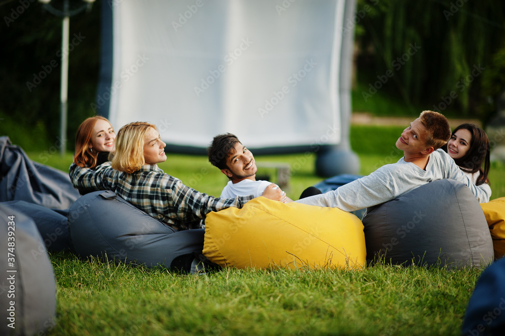 Young multi ethnic group of people watching movie at poof in open air ...